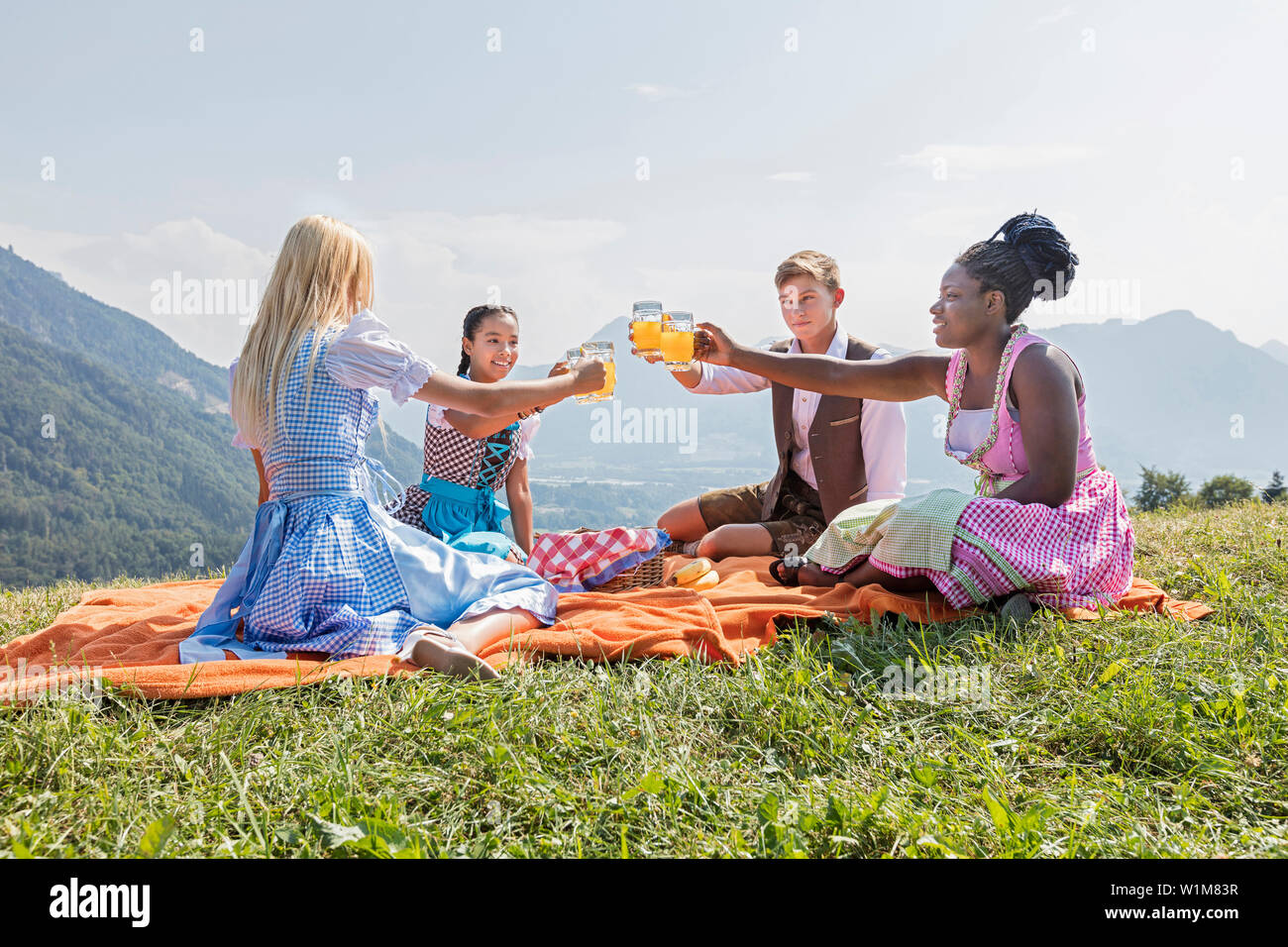 Teenage friends clinking glasses of orange juice during picnic, Bavaria ...