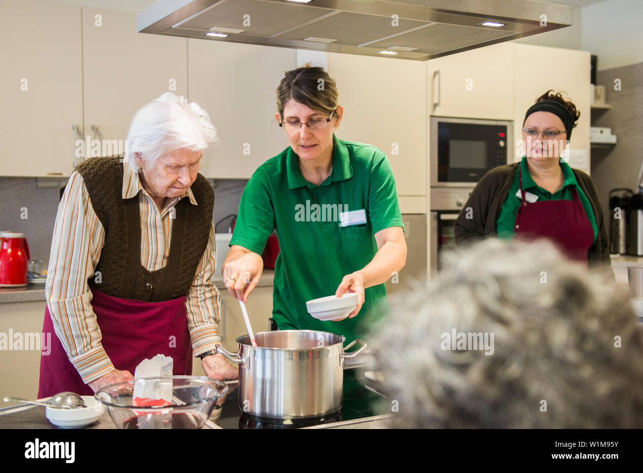 Nursing staff assisting senior woman cooking in rest home Stock Photo ...