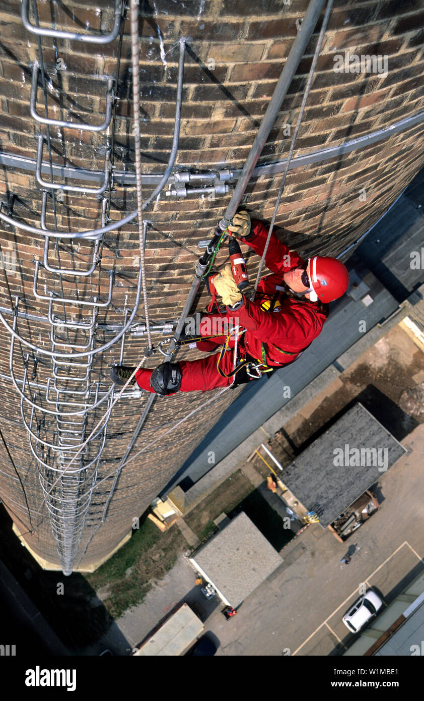 Secured worker climbing up factory chimney, Renovation works on factory ...