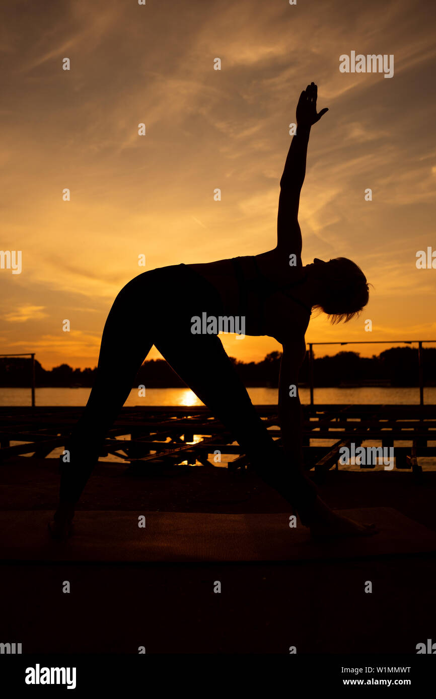 Woman practicing yoga in sunset. Trikonasana, Bikram triangle right ...
