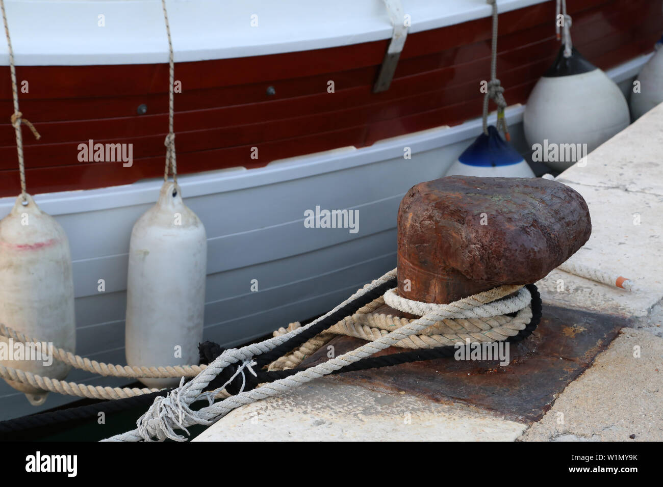 Bollard with a mooring line wrapped around it. Moored boats at the ...