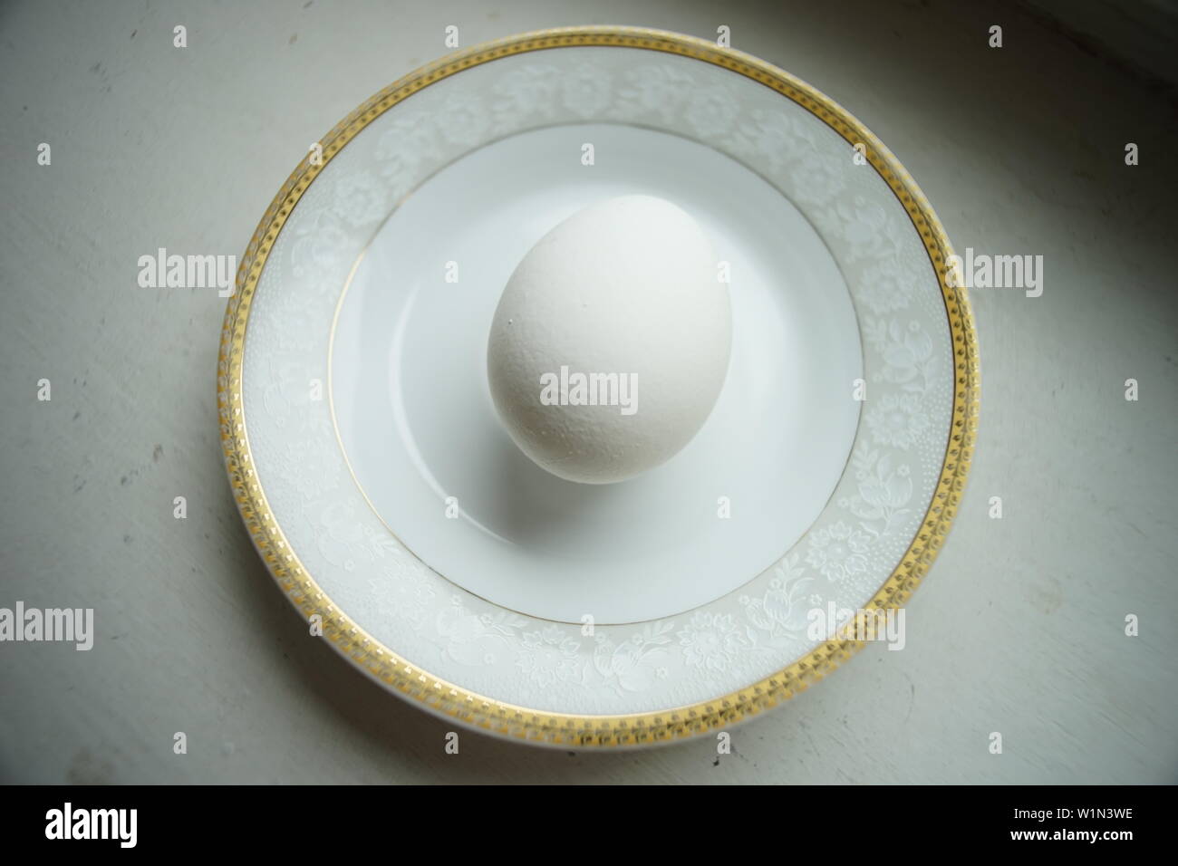 One white boiled chicken egg lies in a small saucer with a gold border ...