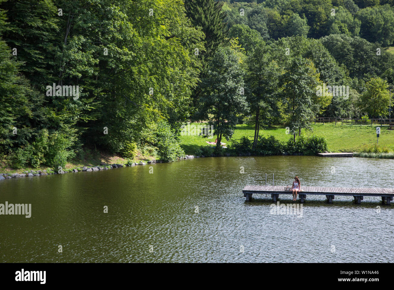 Young woman relaxes on pier at Lake Guckaisee below Wasserkuppe ...