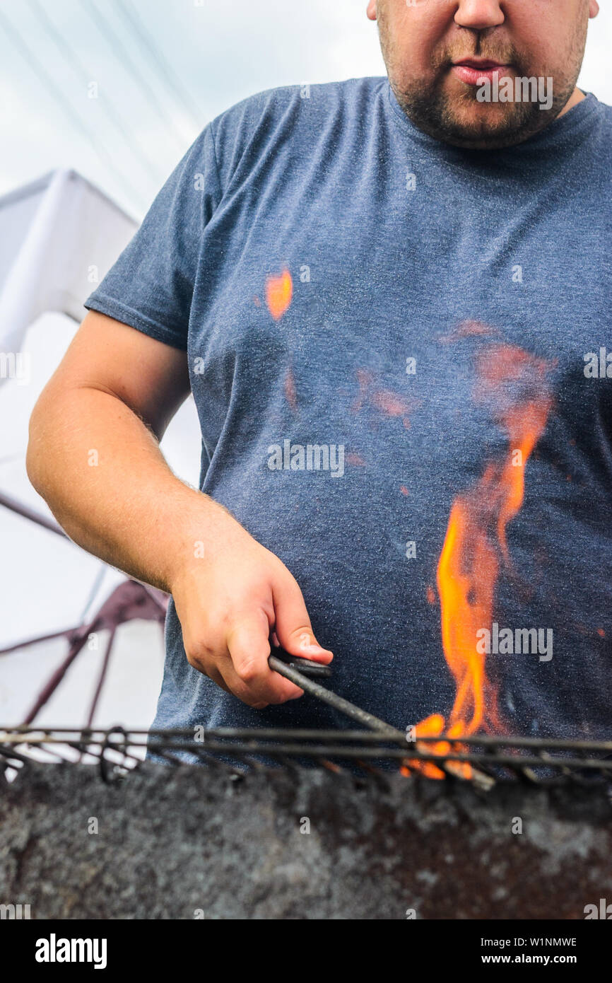 Fat man is cooking on the grill on the street. High flame erupting on ...