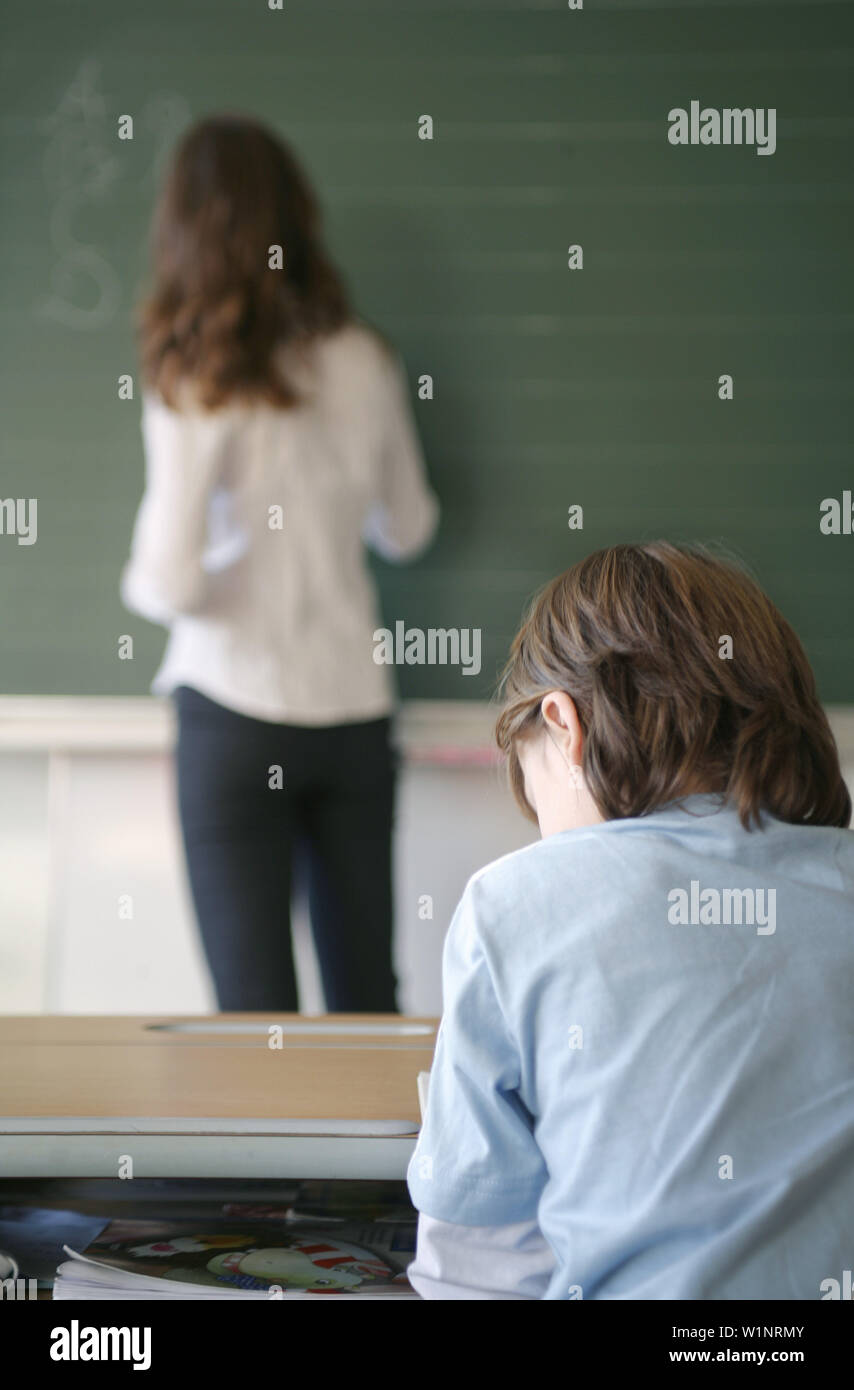 Boy sitting in classroom, teacher standing at blackboard Stock Photo ...