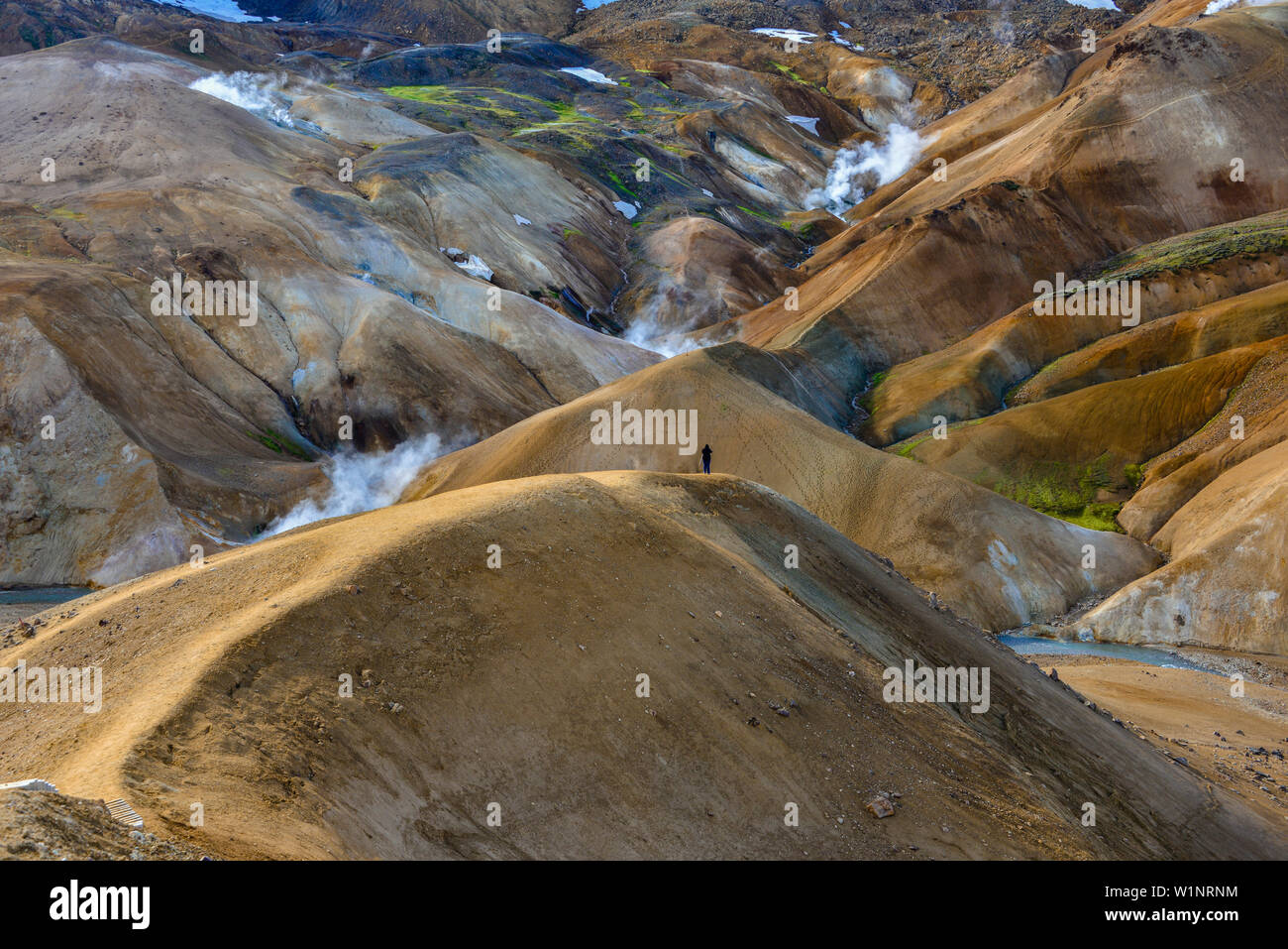 Hiker in Hveradalir, steam is rising out of colorful rhyolith mountains ...