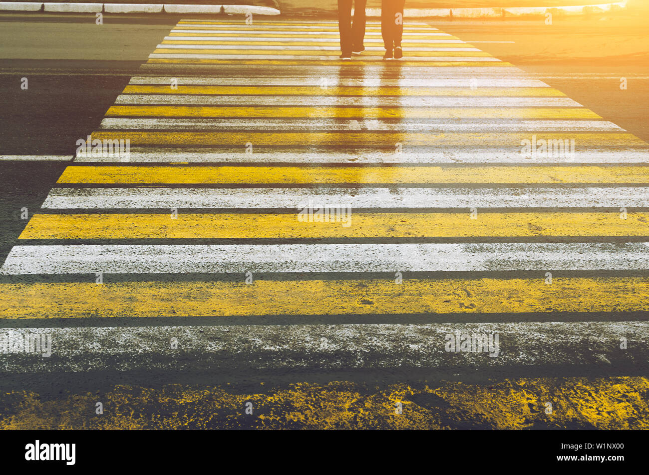 Two people cross a wet road after a rain through a pedestrian crossing ...