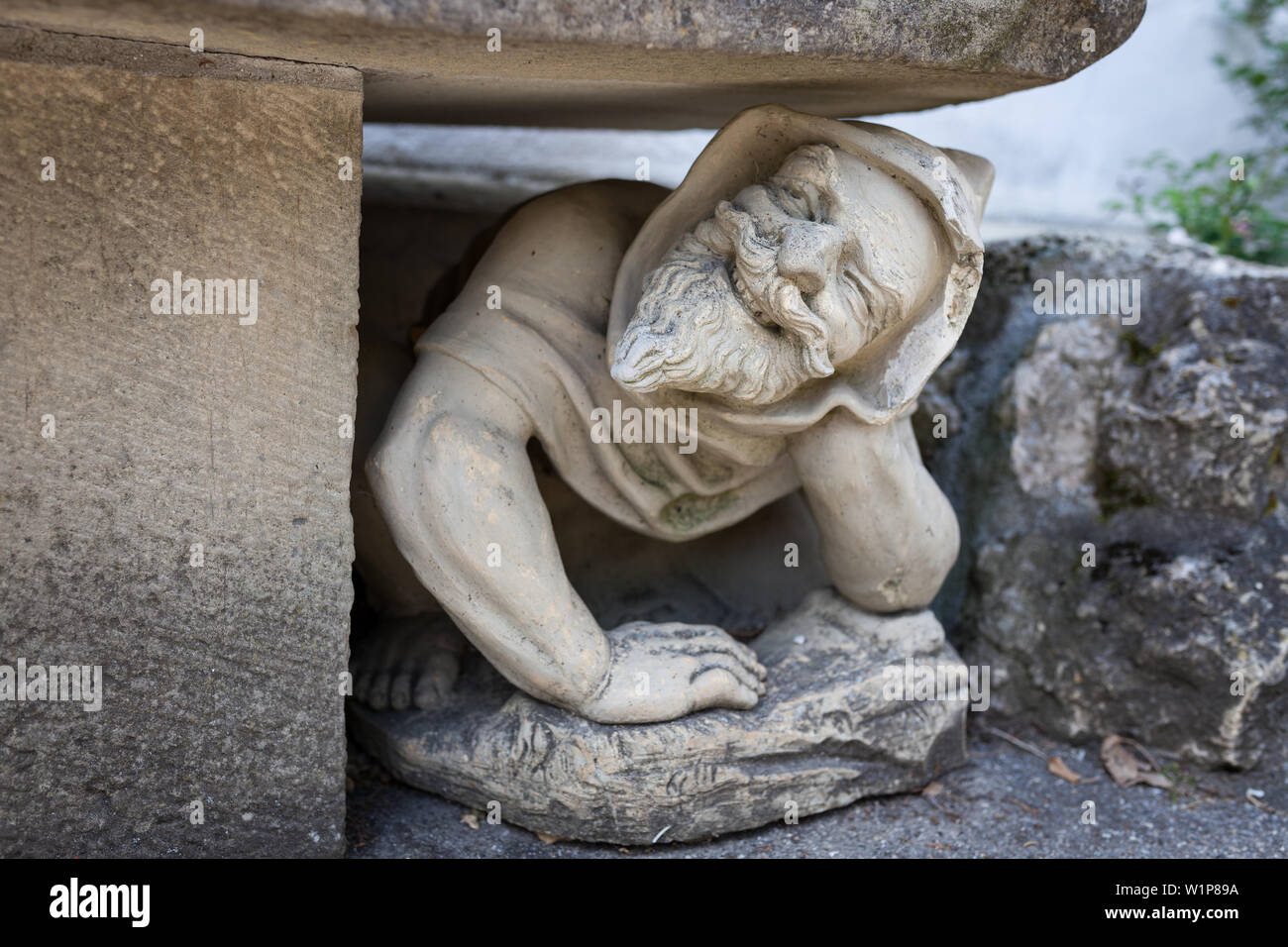Funny human statue crouching under bench in garden Stock Photo - Alamy