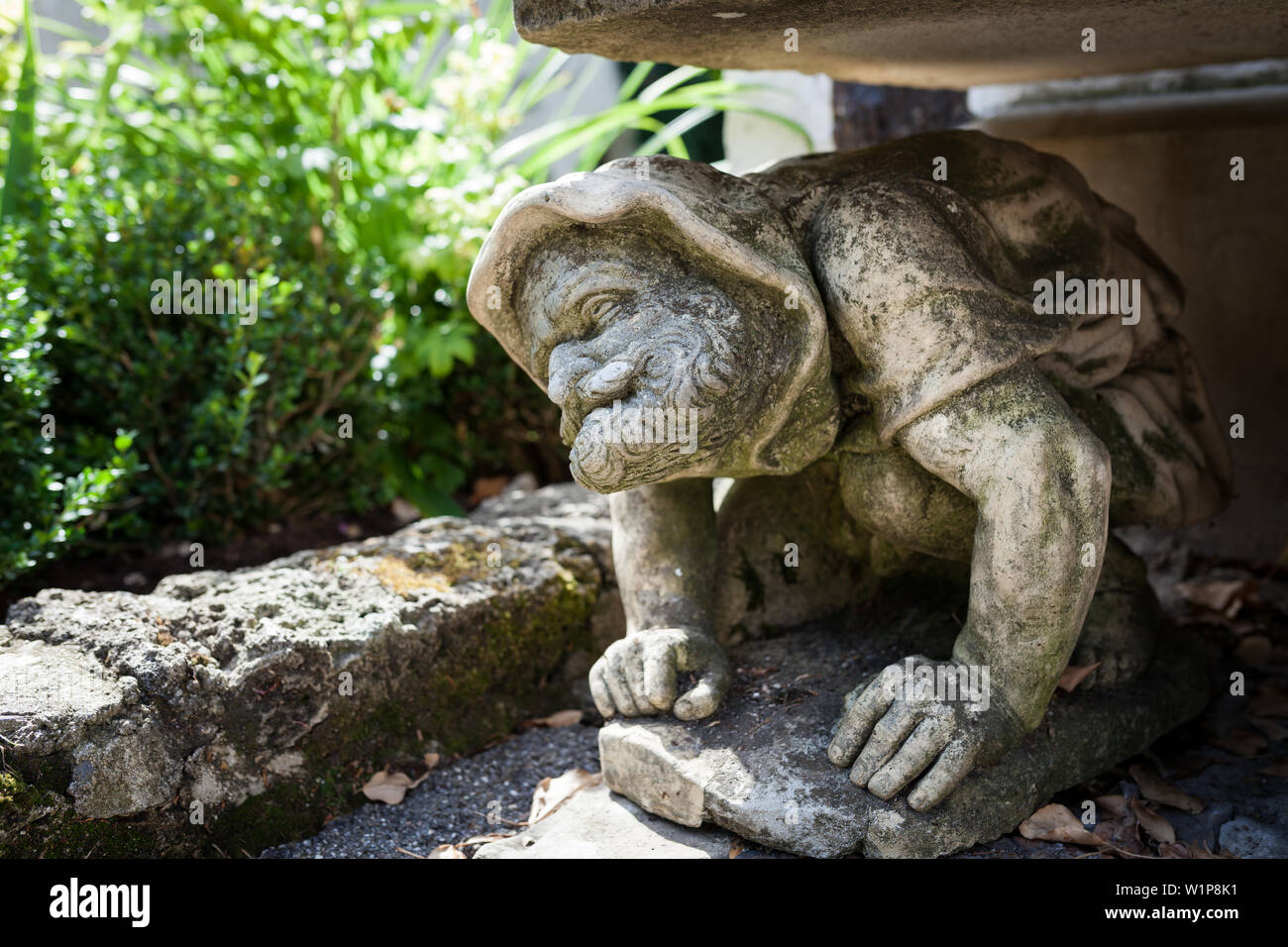 Funny human statue crouching under bench in garden Stock Photo - Alamy