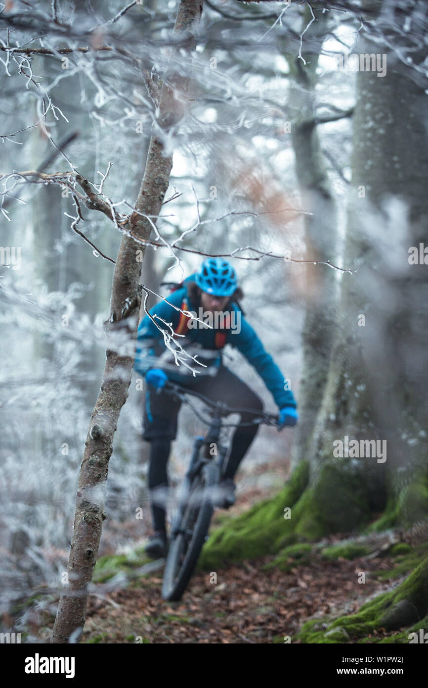 Young man riding with his bike through a with frost covered forest ...
