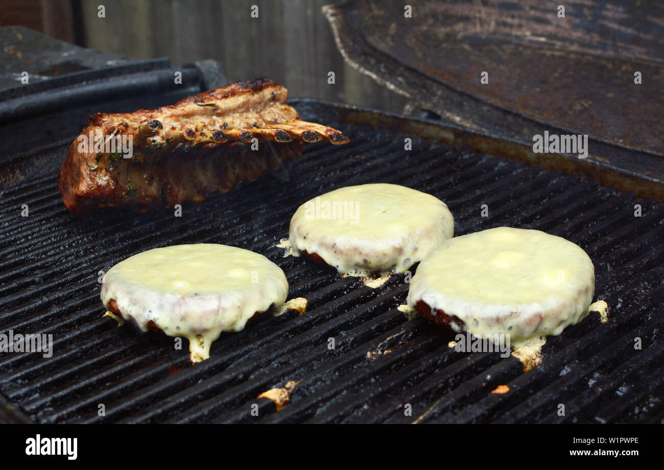 Three cheeseburgers and a rack of lamb finish cooking on a barbecue ...