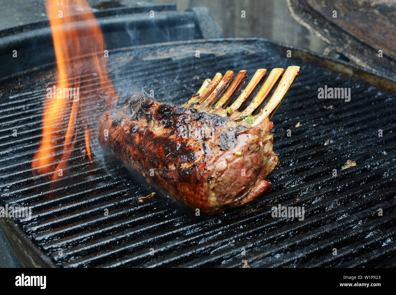 Flame rises from a grill around barbecued meat - a rack of lamb with 7 ...