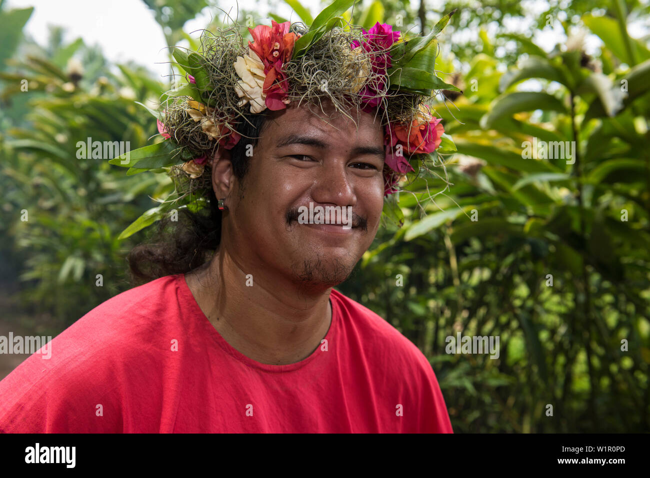 A young man, wearing a red t-shirt and a headdress made of flowers ...