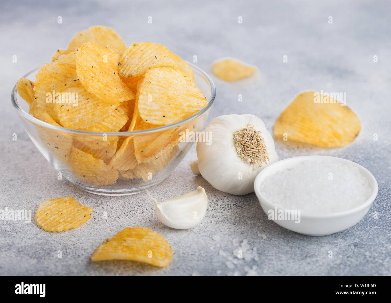 Glass bowl plate with potato crisps chips with garlic and salt on light ...