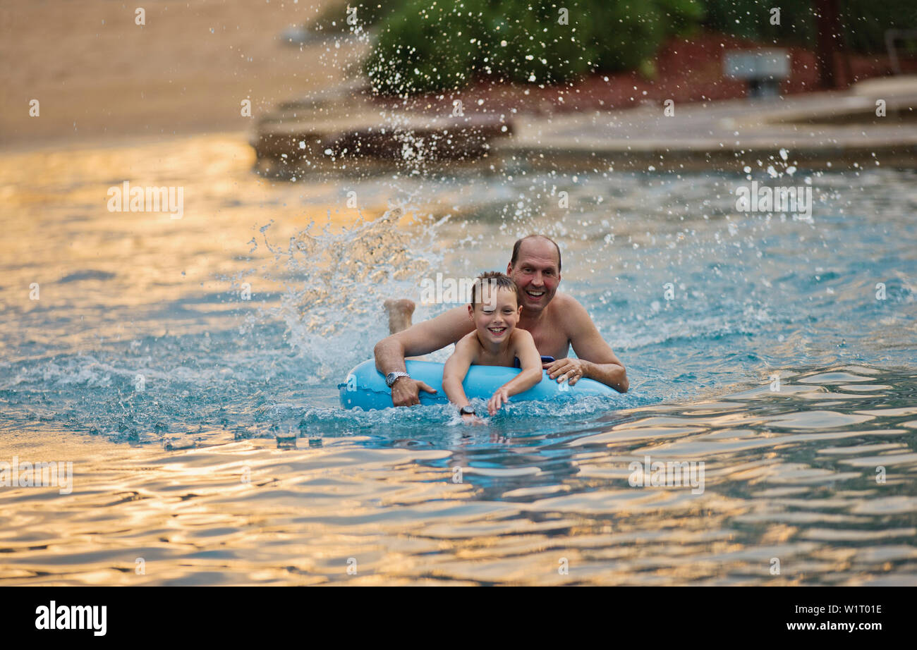 Father and his young son have fun together inner tubing on the lake ...