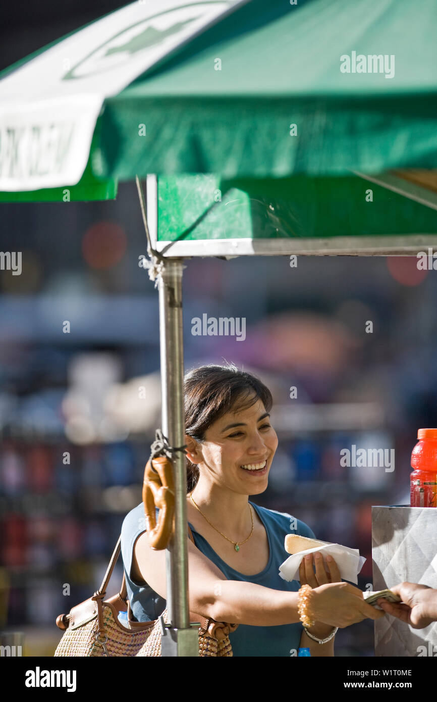 Smiling mid-adult woman handing over money at a hotdog stall in the ...