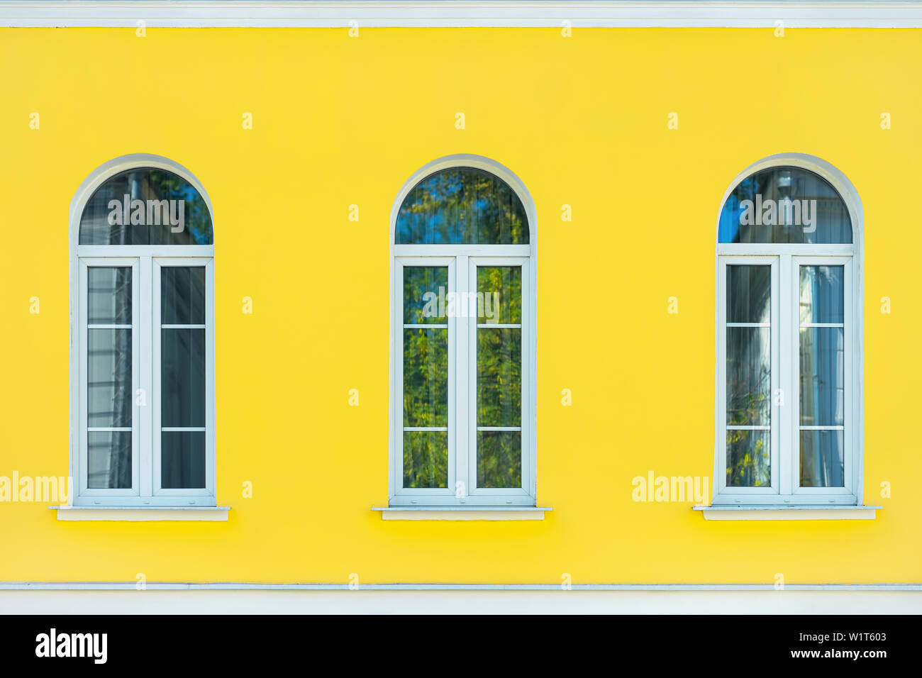 Windows on the bright yellow wall, front view. Colorful architecture ...