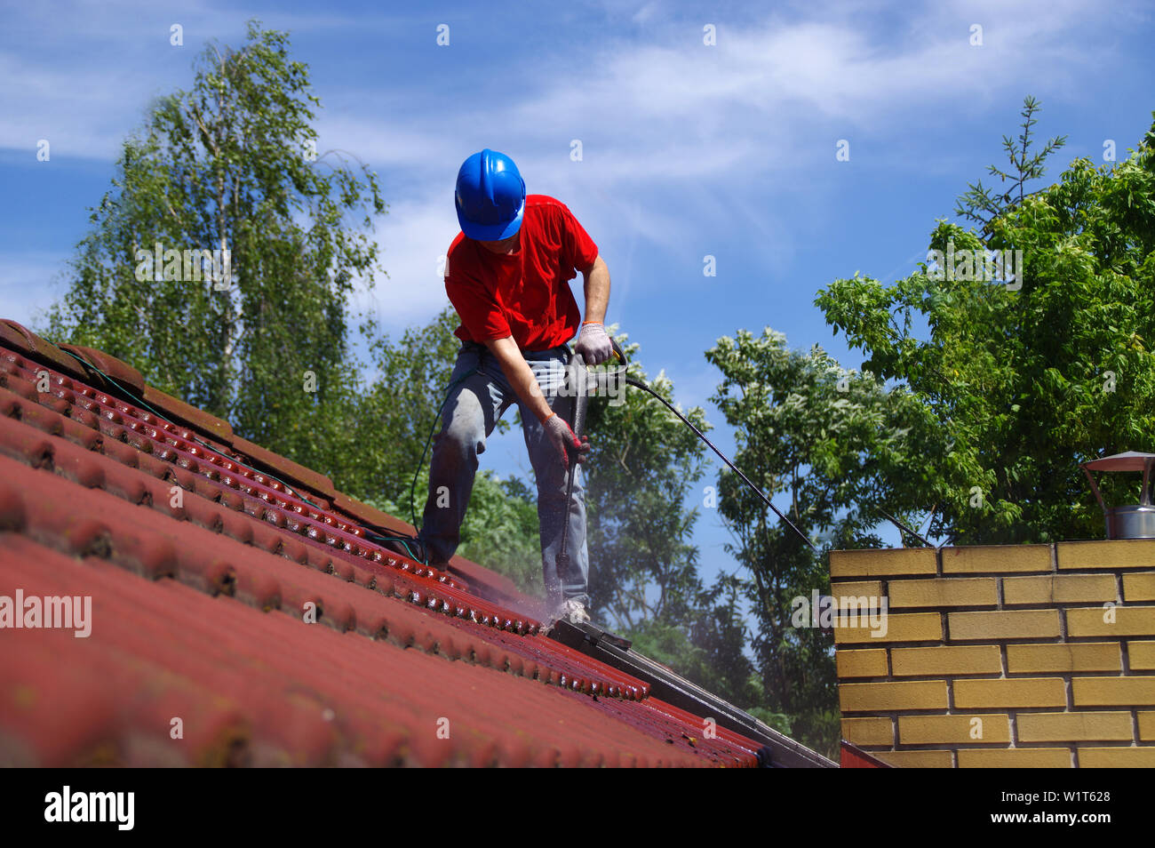 House roof cleaning with pressure tool. Worker on top of building ...