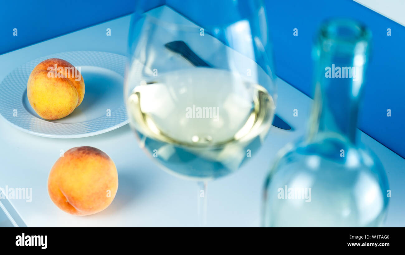 Dining table still life with white wine and ripe peaches. Glassware ...