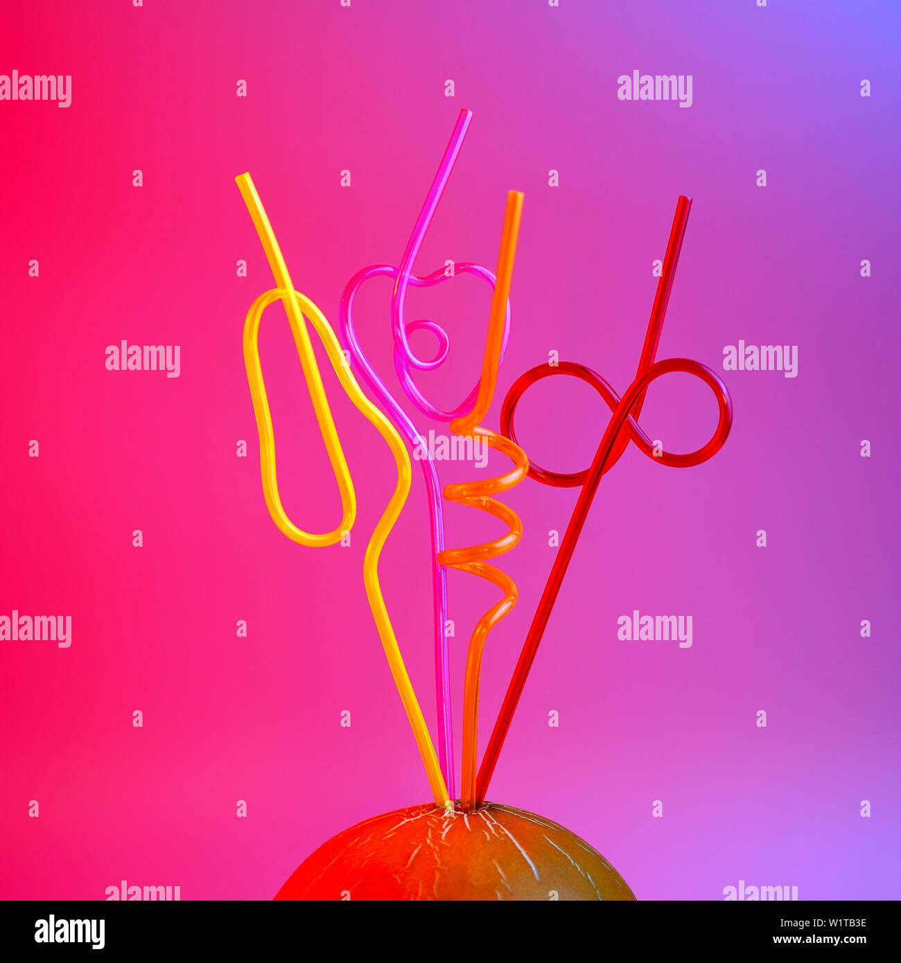 bright colored cocktail tubes stuck in a melon on a pink background ...