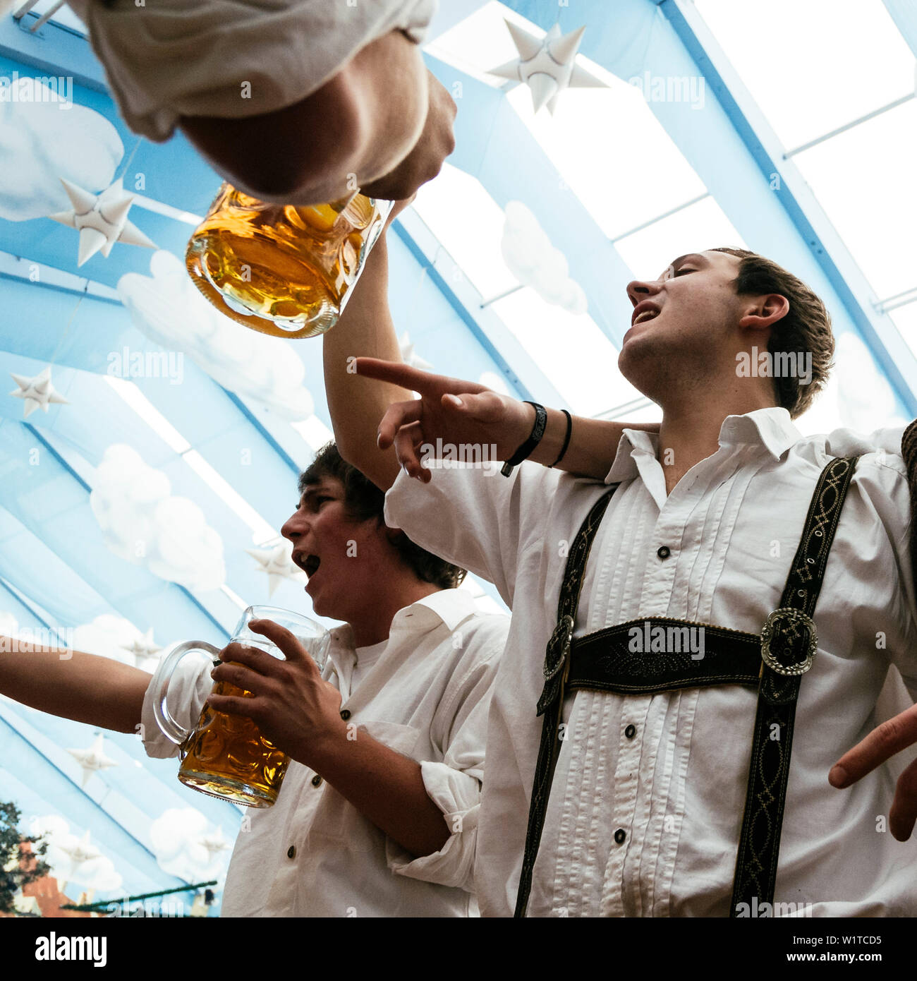 Young men in leather trousers standing on beer benches celebrate ...