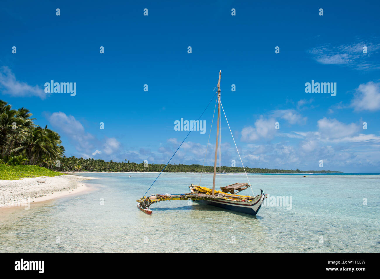 A lone single-outrigger boat with mast rests just offshore among coral ...