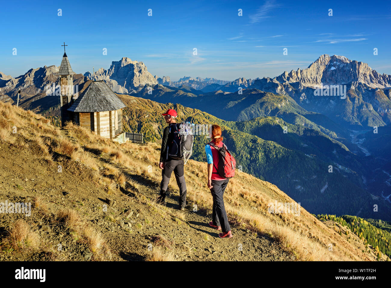 Man and woman hiking towards chapel, Monte Pelmo and Civetta in ...