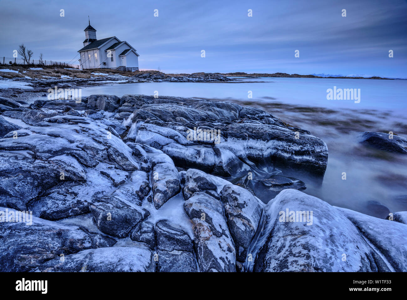 Icy rocks at beach with church in background, Gimsoy, Lofoten, Nordland ...