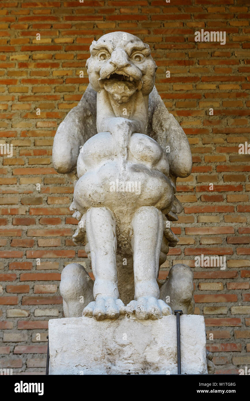 front view of a gargoyle carved in stone with a wall of bricks as ...