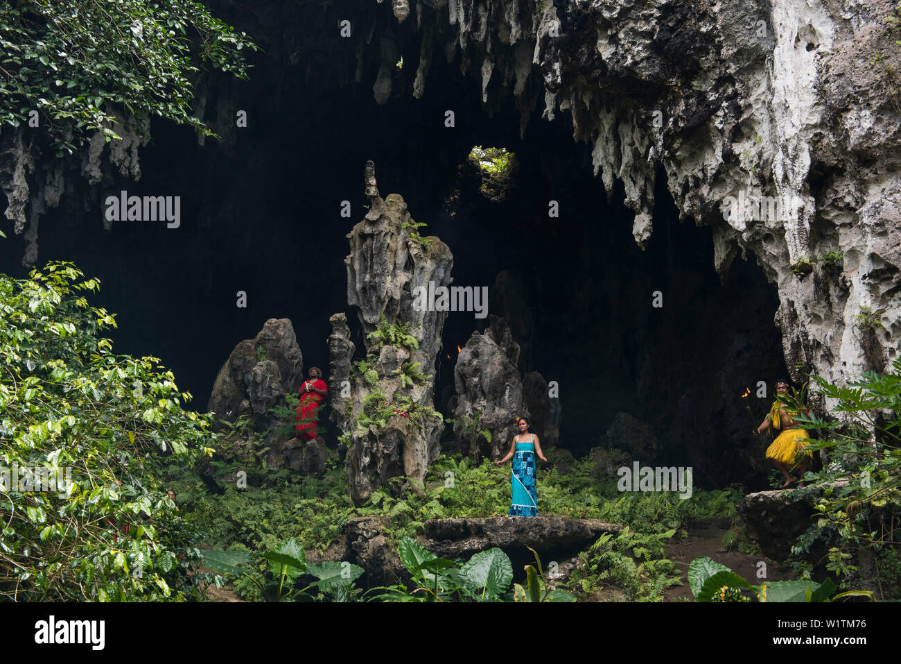 Two men and a woman wearing colorful clothing stand in the mouth of a ...