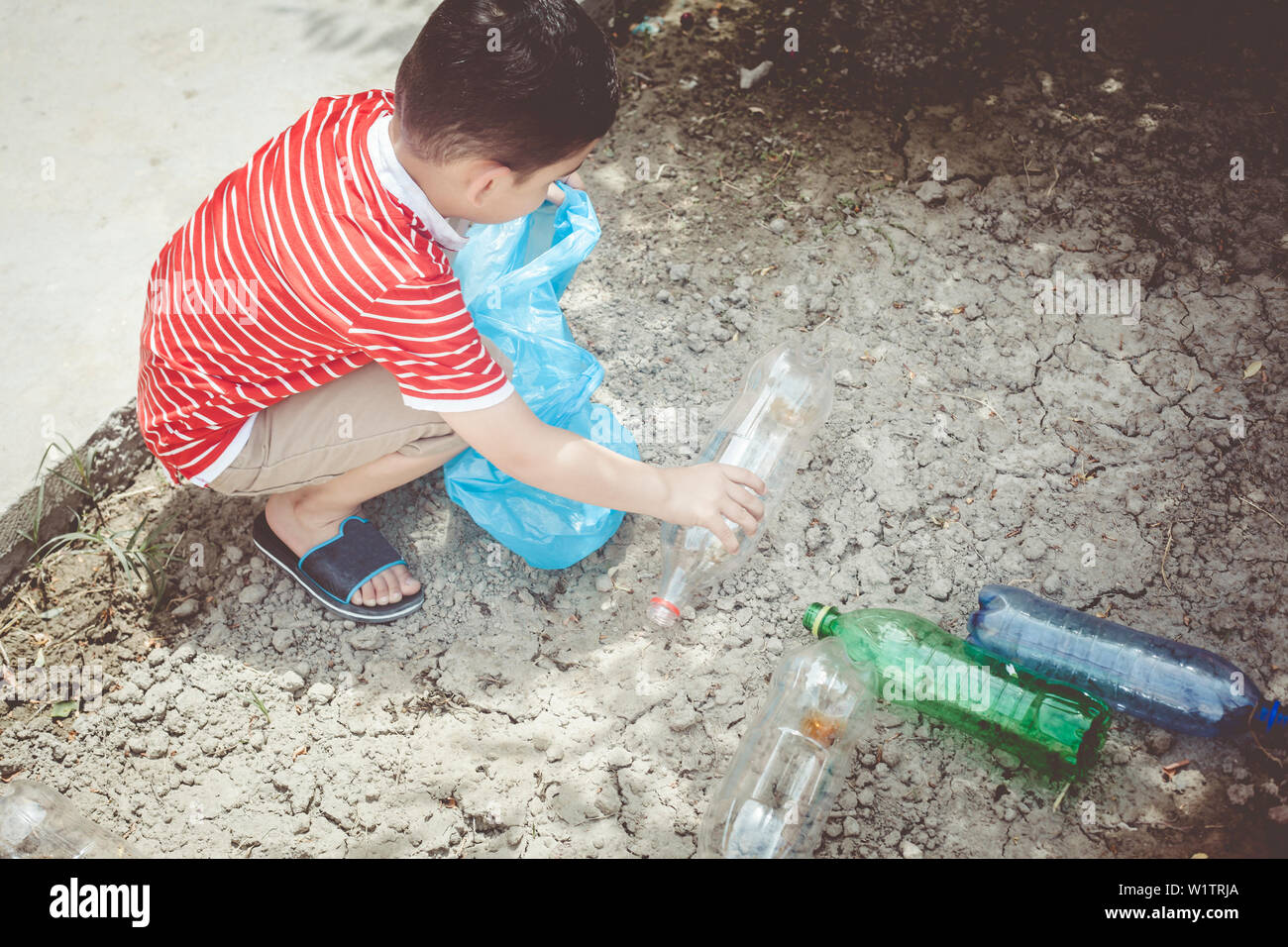 Plastic pollution on land. Little boy collecting plastic bottles. Kid ...