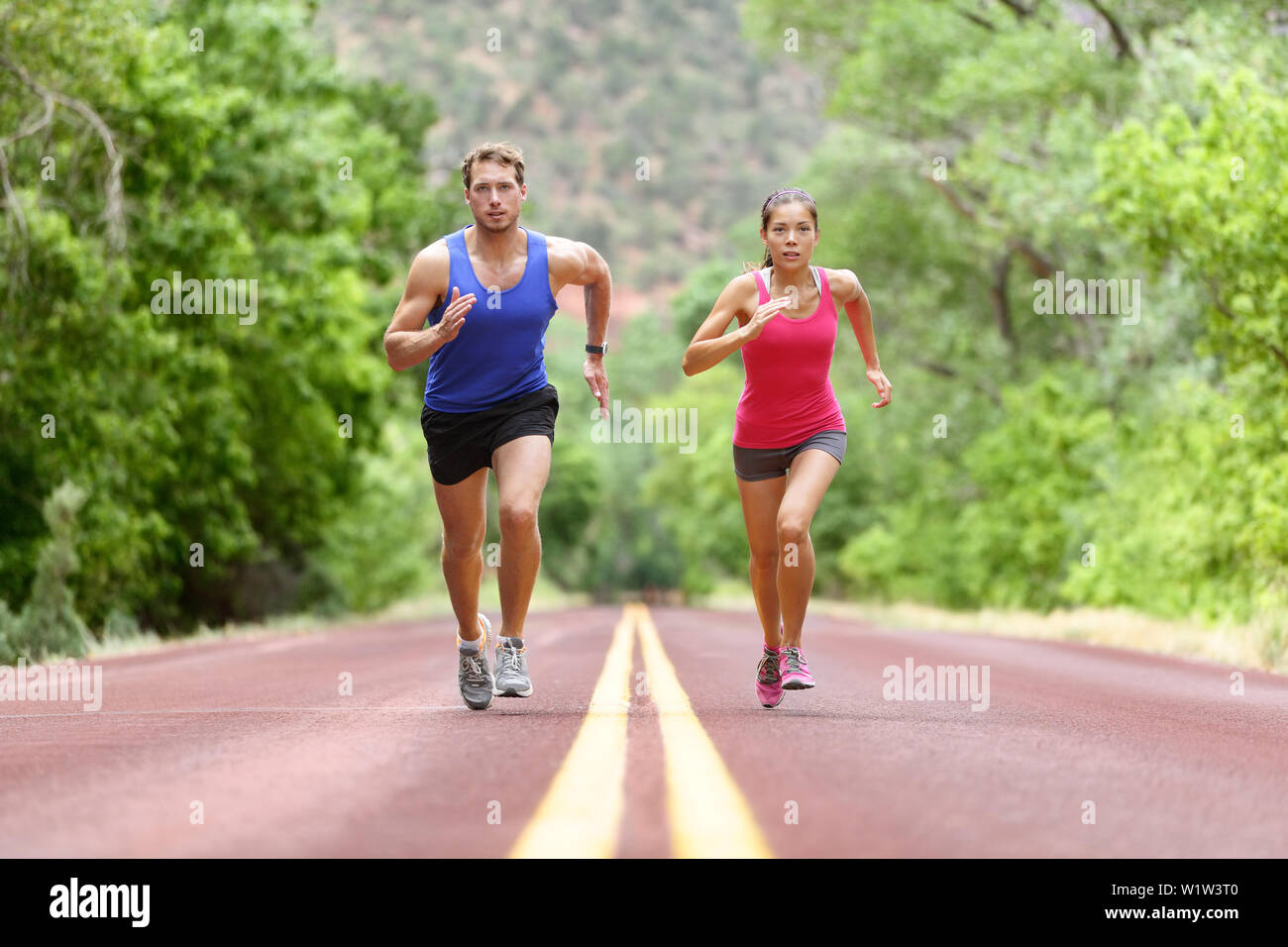 Determined man and woman running on road against trees. Runners ...
