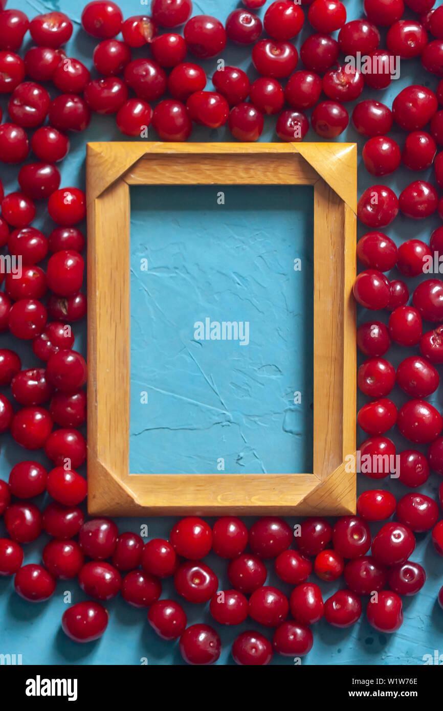 Wooden frame with free space and ripe cherries on blue background ...
