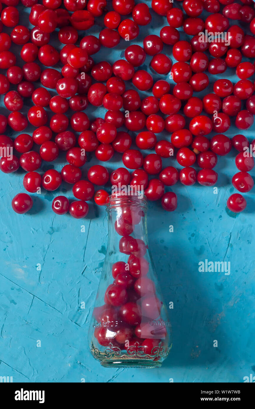 Pile of ripe cherries and glass bottle on blue background. Fresh ...