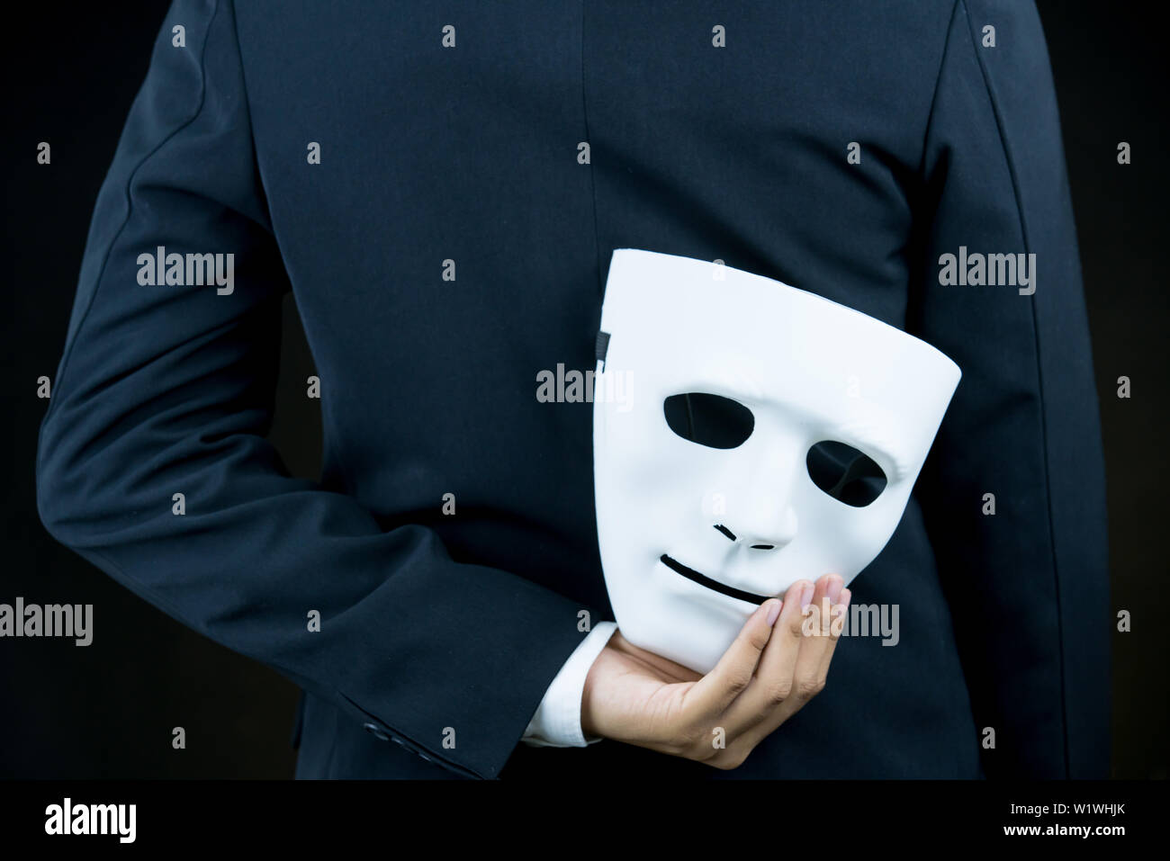 businessman hide the white mask in the hand behind his back on black ...