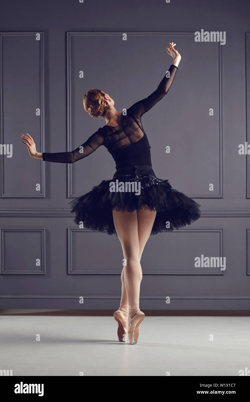 Ballerina ballet dancer in black dress posing over gray background back ...