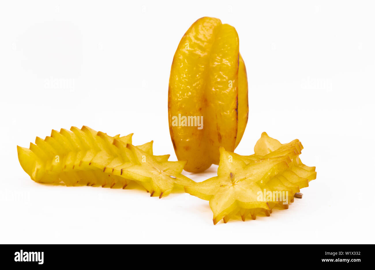 A whole star fruit next to two piles of ripe star fruit cut on a white ...