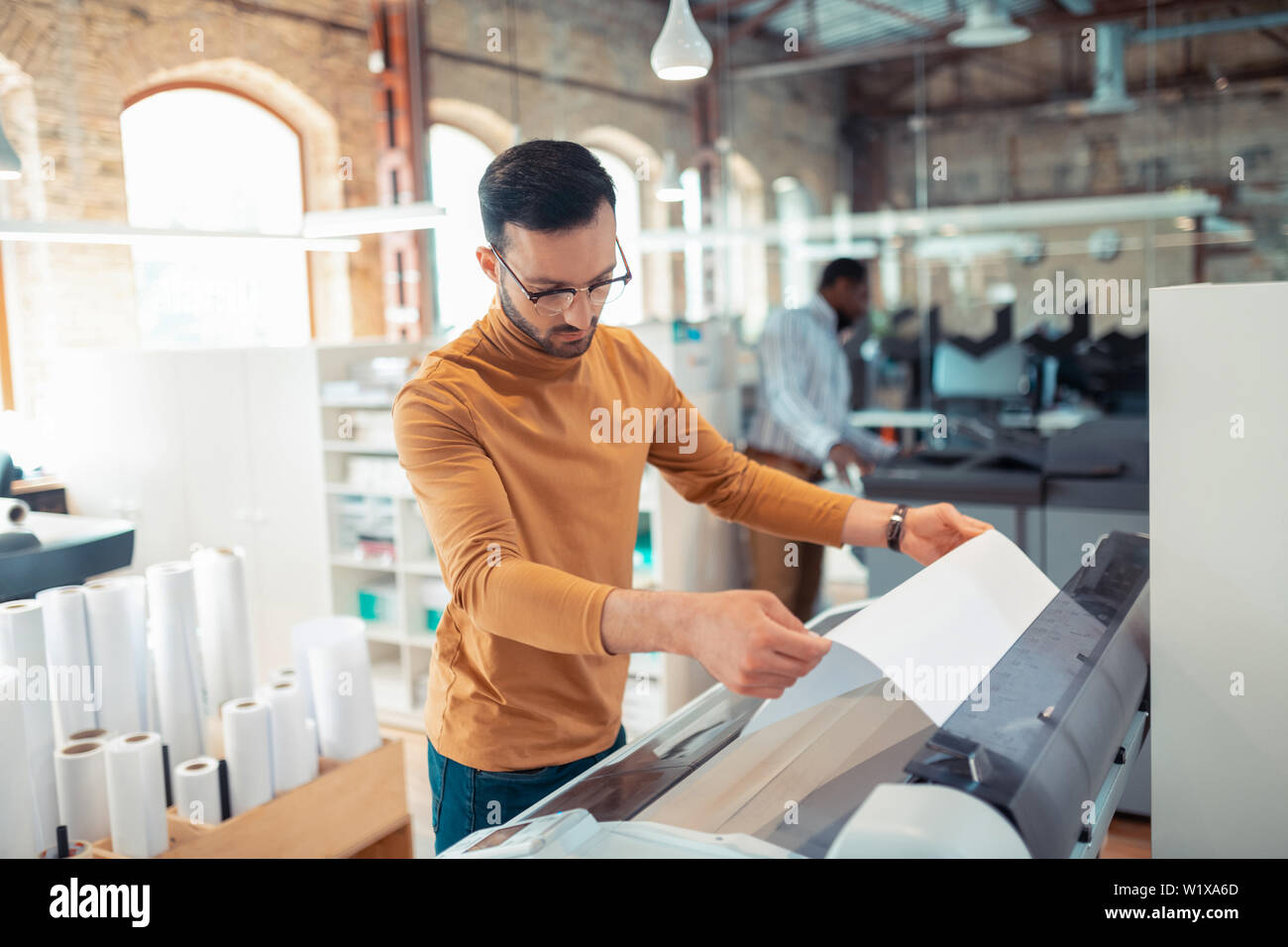 Printing posters. Bearded man feeling busy while printing posters for ...