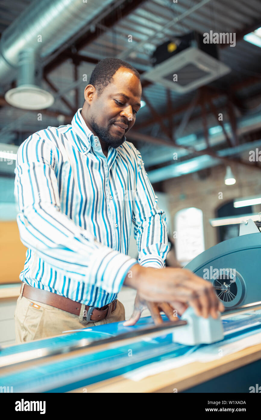 Paper manufacturing. Dark-skinned man wearing striped shirt working ...
