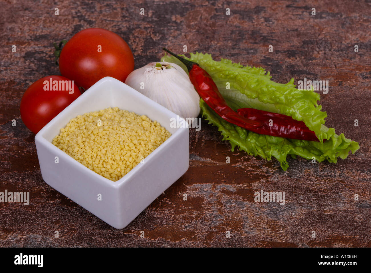 Raw couscous in the bowl served salad leaves, tomato and pepper ready ...