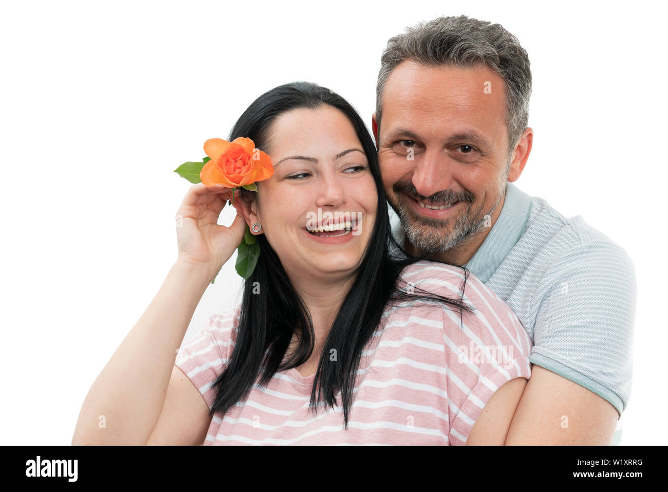 Joyful man hugging happy woman with orange rose behind ear as couple ...