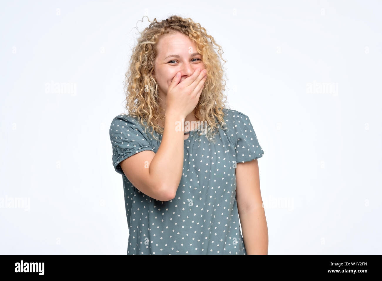 Good looking young female giggles joyfully, covers mouth as tries stop ...