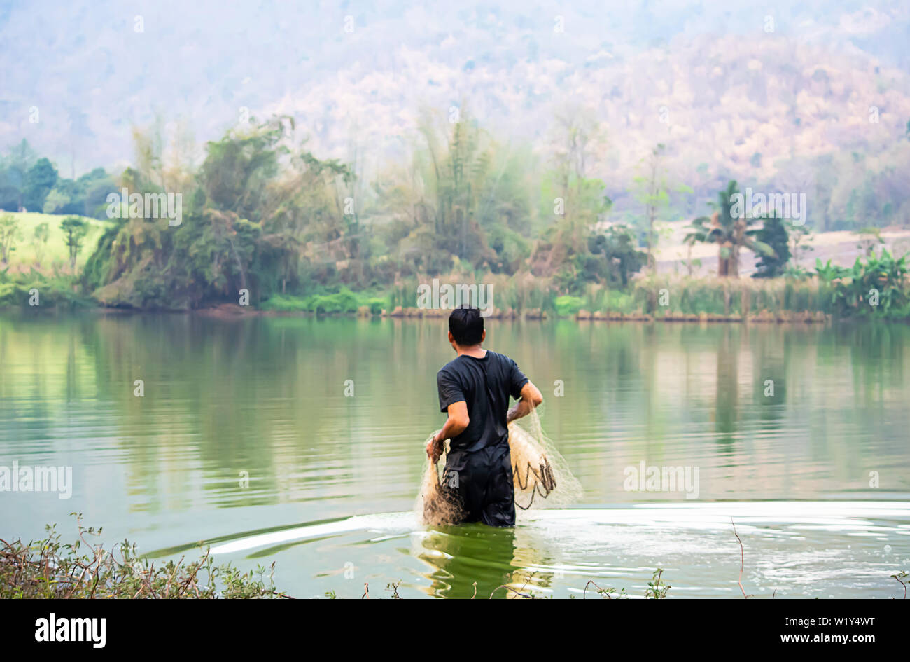 Man holding fishing nets walking in water Background blurred mountains ...