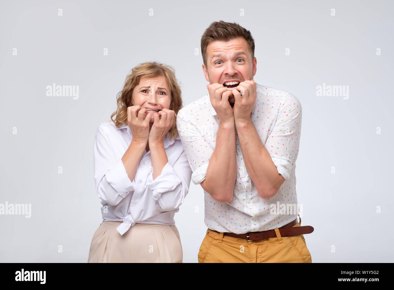 Scared man and woman biting their nails feeling stressed and surprised ...