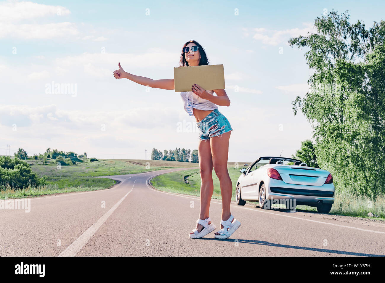 Smiling woman hitchhiker on the road is holding a blank board. Concept ...