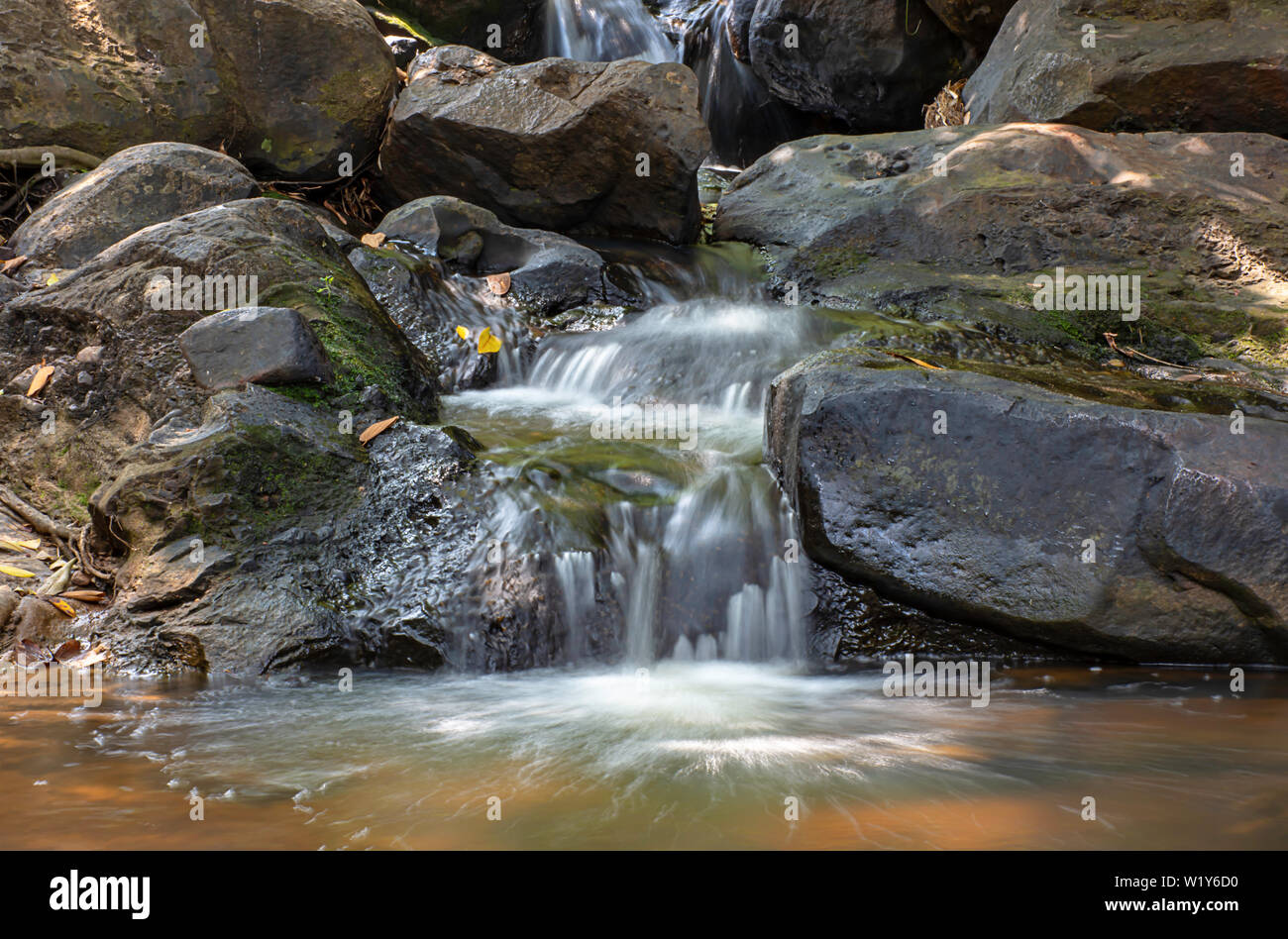 The water flowing over rocks and trees down a waterfall at Khao Ito ...
