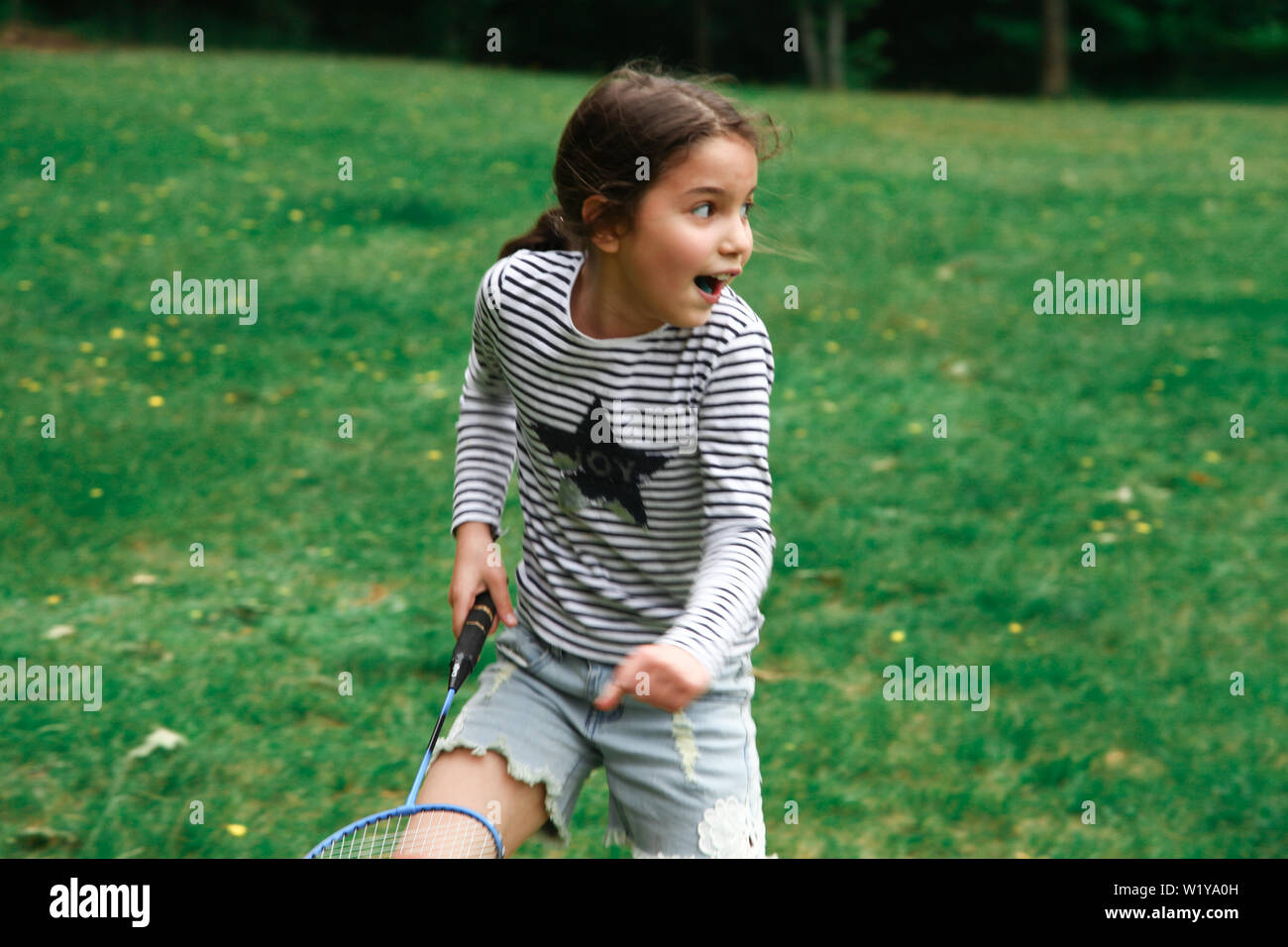 Young girl playing badminton outdoors. She holding a racket and a ...