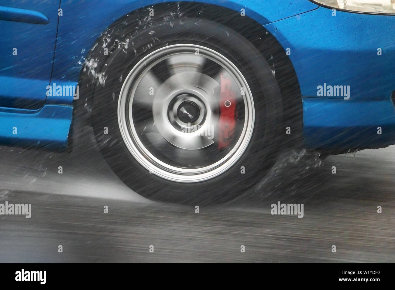 Detail of the wheel of a car driving in the rain on a wet road ...