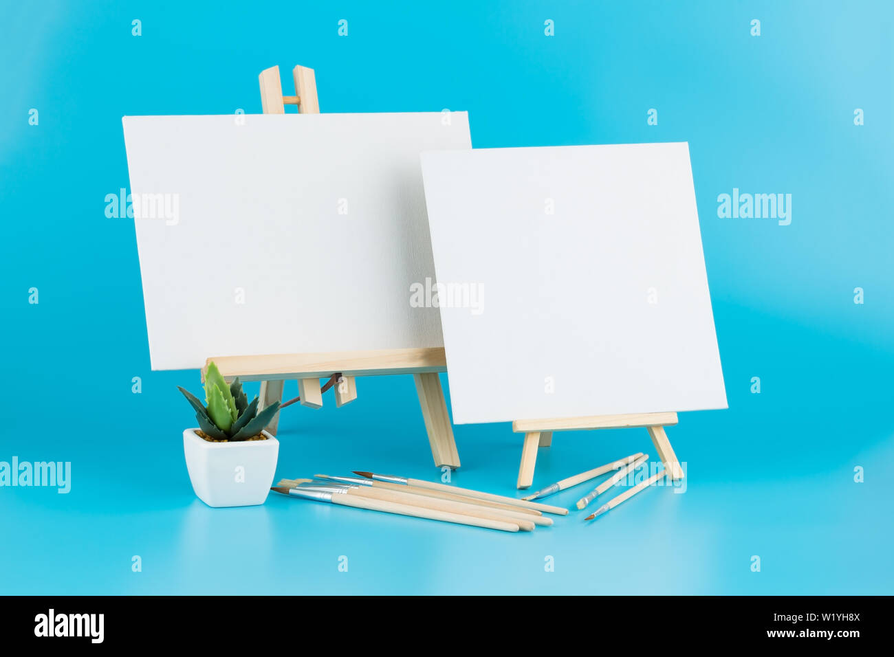 Two wooden blank easels with brushes and plant on blue background Stock ...
