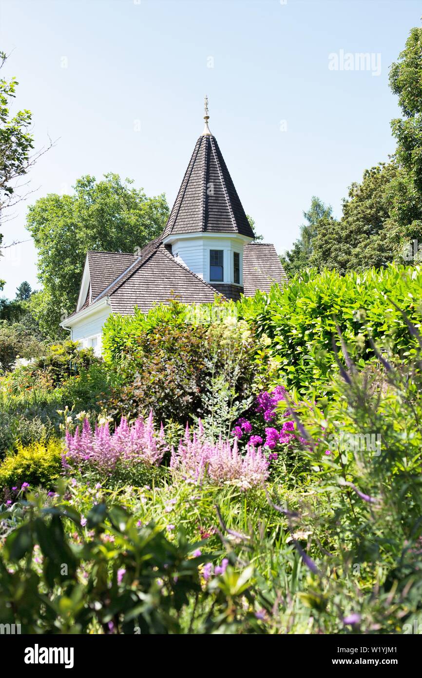 The roof of a Queen Anne victorian home behind lush gardens, at ...